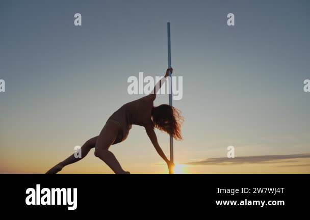 pole dance. silhouette. fit female gymnast, in beige leotard, performs ...
