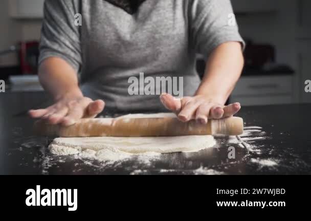 Woman rolling out dough in flour on a black counter top. Lady in gray ...