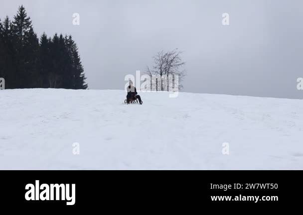 Man from the village in black winter clothes rides down the slope on a ...