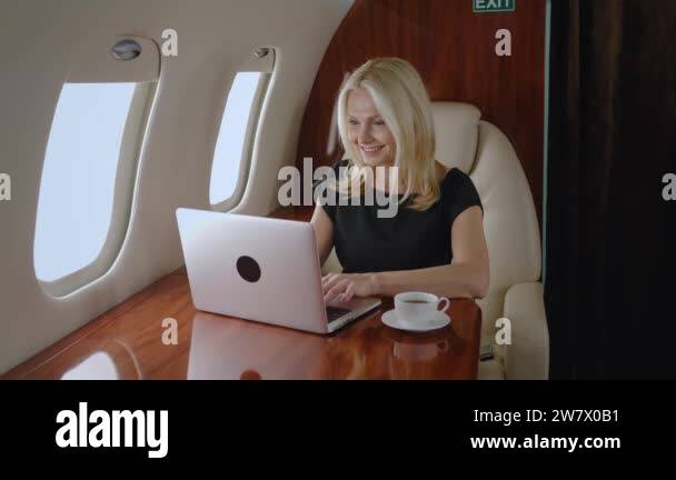 Beautiful mature woman millionaire in airplane working at laptop and ...