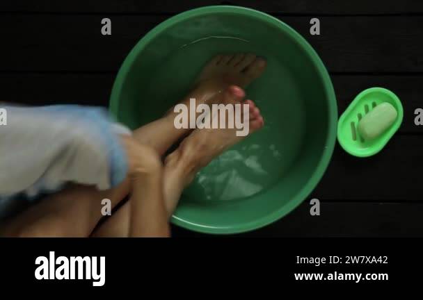 girl washes her feet in a bowl of water on the wooden floor at home ...
