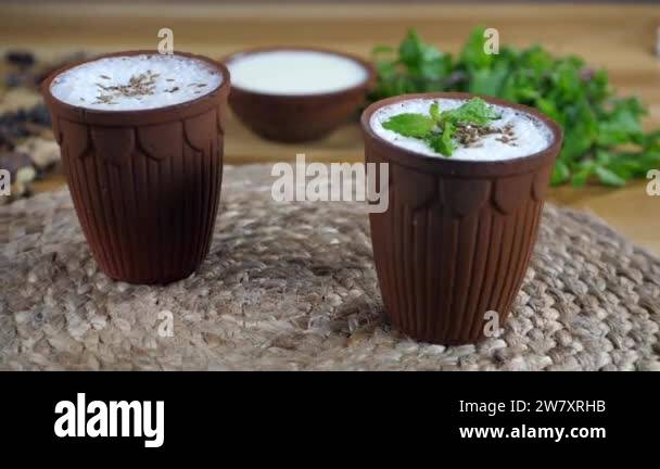 Two glasses of Chaas seasoned with cumin seeds and mint leaves rotating ...