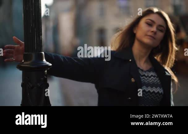 Young charming girl with natural make-up is coming to the street lamp ...