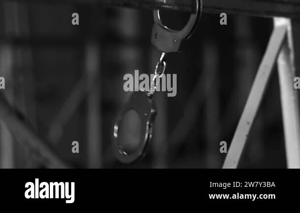 Handcuffs swinging on the handrail on a prison background, black and ...
