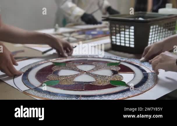 Two artists assemble a composition from stained glass details. Hands of two women. Craft ...