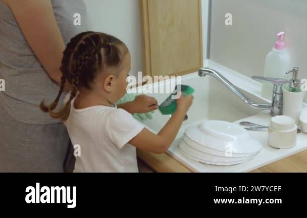 Mother and small daughter wash spoon and dishes in kitchen. Young ...
