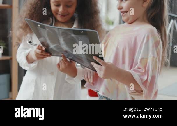 Handheld slowmo of laughing 8-year-old girls playing doctor and looking ...