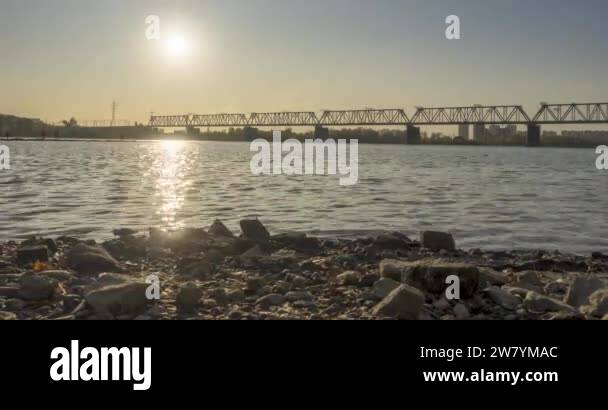 Timelapse of city river bank. Sun rays, blue sky and railway bridge ...
