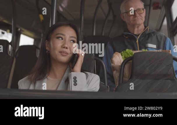Chest-up of young Asian woman talking on mobile phone sitting in public ...