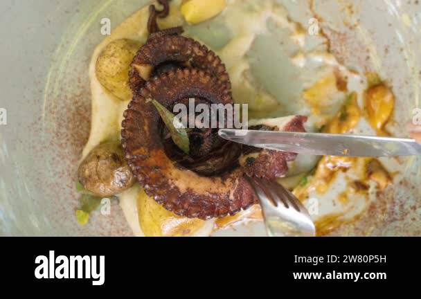 Female hands holding cutlery and cutting off a piece of grilled octopus ...