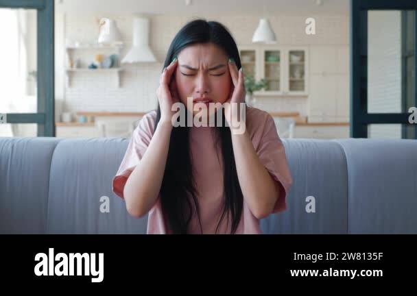 Frustrated deappointed and upset young Asian woman sitting on the couch ...