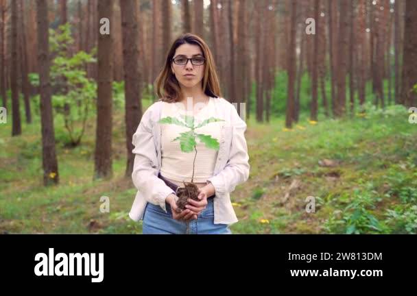 portrait of a young student girl with an oak sapling plant in her hands ...