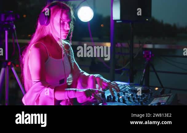 Cool dj is working in a nightclub, standing at turntables, creating a ...