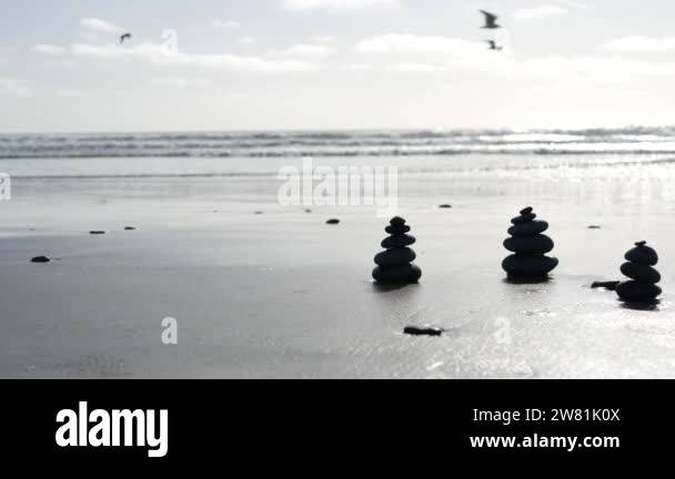Rock balancing on ocean beach, stones stacking by sea water waves ...
