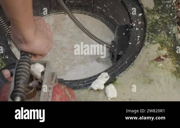 Drain cleaning. Plumber repairing clogged grease trap with auger ...
