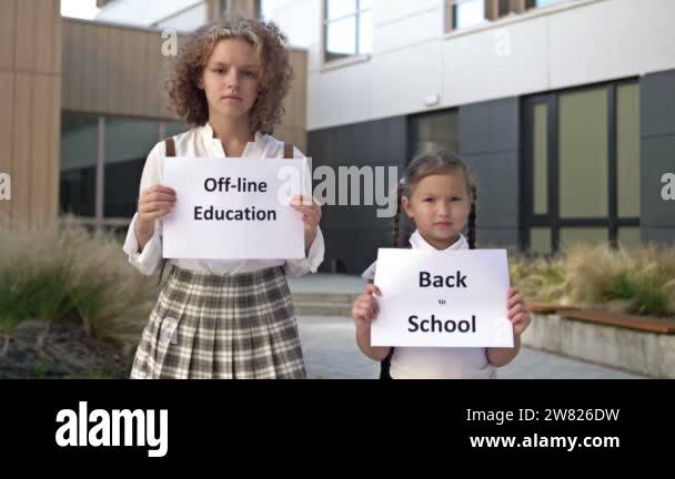 Two schoolgirls with placards are standing in front of the school ...