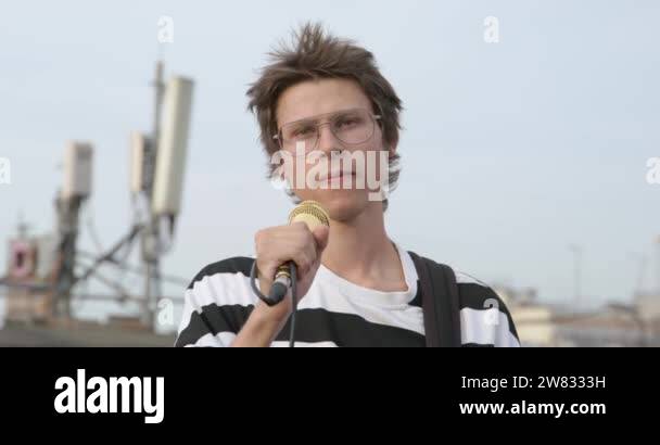 Young guy with glasses and nose piercing holds microphone on a stand ...