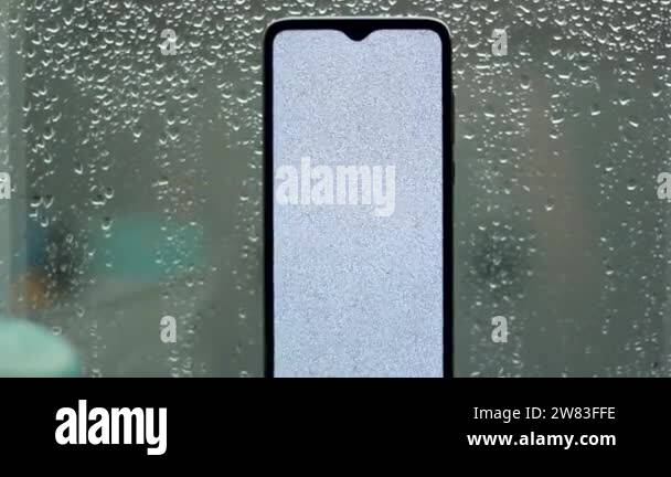 White Noise TV animation on mobile phone against glass window with dew ...