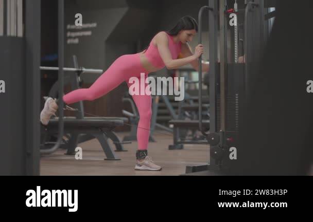 A young woman lifts her leg in a crossover to train her thigh and leg ...