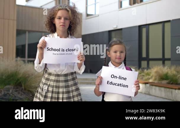 Two schoolgirls with placards are standing in front of the school ...