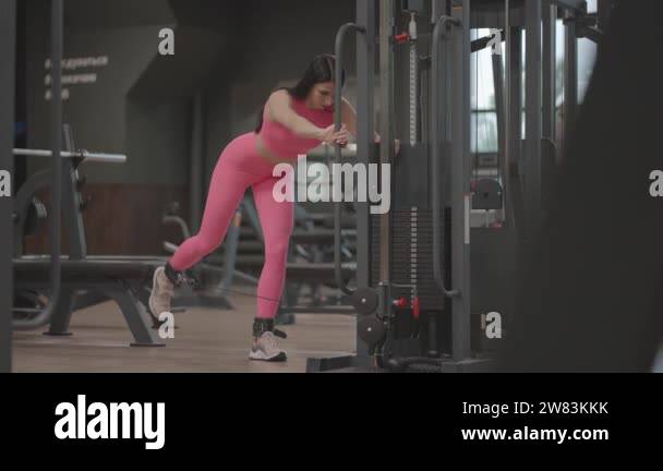 A young woman lifts her leg in a crossover to train her thigh and leg ...