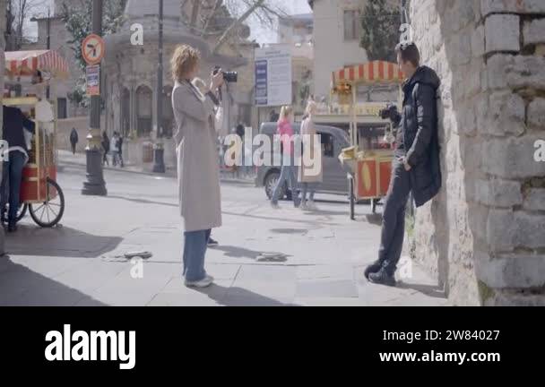 Woman photographs young man in old European city. Action. Side view of ...