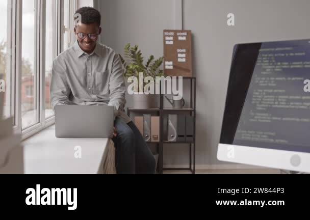 Medium stab shot of young male African-American programmer sitting on ...