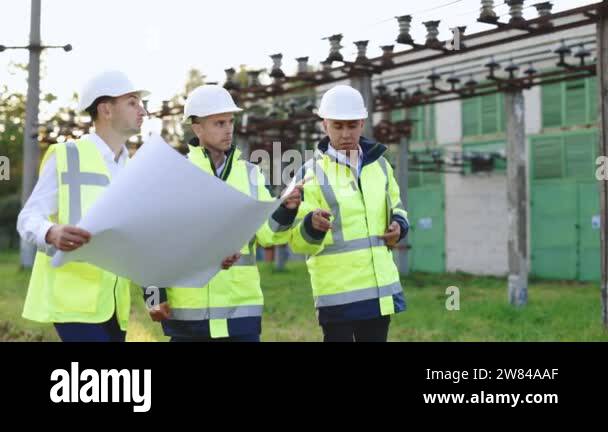 Three engineers walk near power lines in the high voltage power station ...