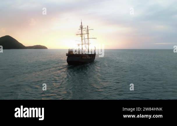 Cinematic back view of historic ship sailing toward scenic pink golden ...