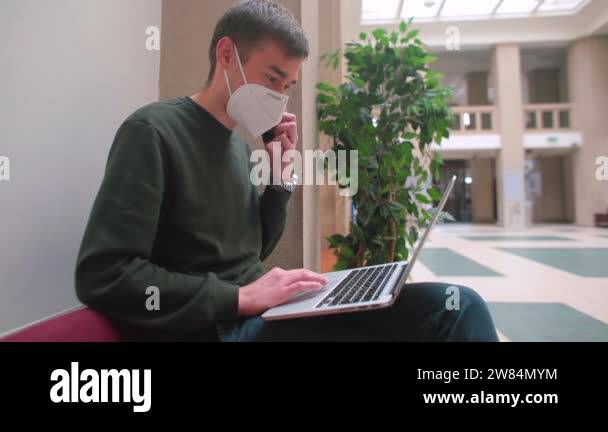 masked man uses laptop and telephone hotel lobby freelance work using ...