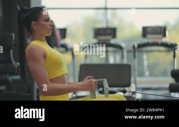 Hispanic Woman Does Exercises On The Rowing Machine A Girl Sits Behind