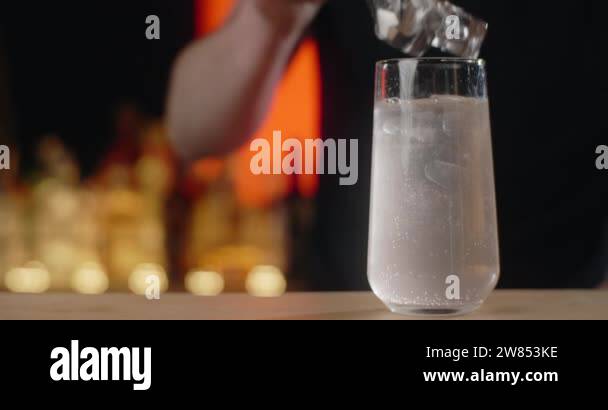 Bartender adds ice cubes to the glass with refreshment beverage in slow motion, making the ...