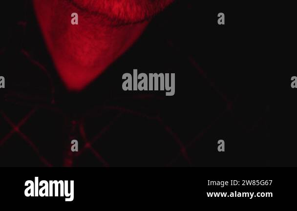 A close-up of an unshaven man's face grinning. Grim red lighting ...