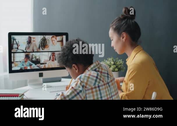 Little Afro-American boy watching online school lesson via video call on computer and taking ...