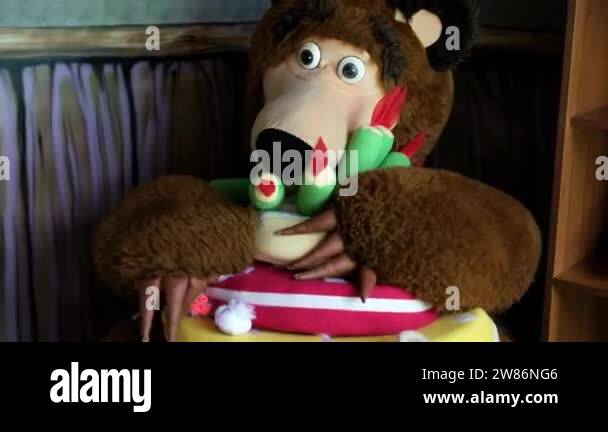 A brown bear life-size puppet sits in a cozy armchair with a large toy ...