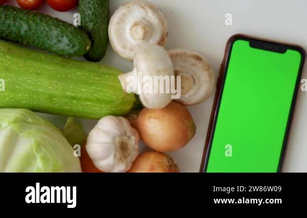 A phone with a green screen is lying on the side of the vegetables and ...