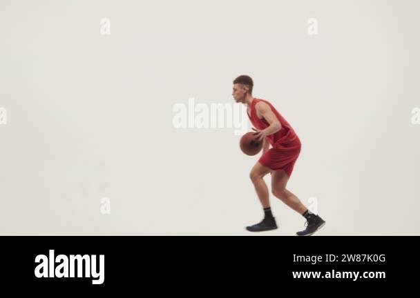Young basketball player in sports uniform runs and dribbles on a white ...
