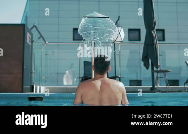 Young guy standing in the pool under the rain shower of a luxury hotel ...