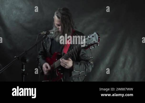 Bearded rock musician in leather jacket plays red electric guitar and ...