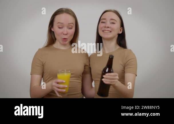 Twins toasting healthful juice and beer bottle smiling looking at ...