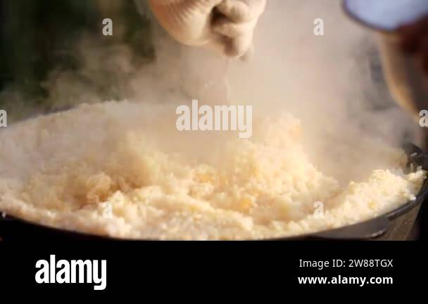 Cook is stirring the rice with a large metal spoon. Lots of steam, rice ...