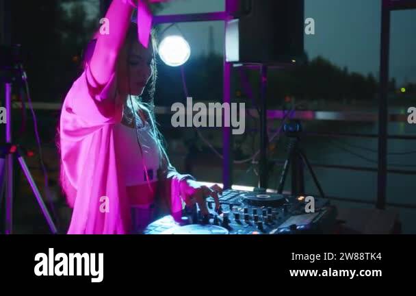 Cool dj is working in a nightclub, standing at turntables, creating a ...