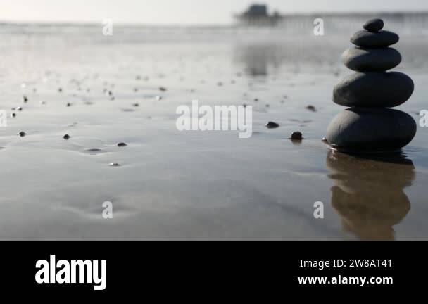 Rock balancing on ocean beach, stones stacking by sea water waves ...