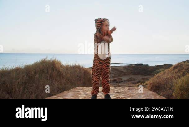 Cute children in a tiger costume at sunny dawn by the sea doing sport ...