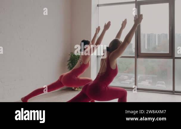 Two women in red sports uniforms make virabhadrasana in yoga studio ...