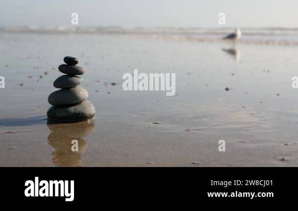 Rock balancing on ocean beach, stones stacking by sea water waves ...