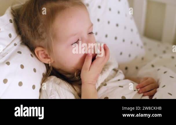 Sick one-year-old child lies in bed and coughs violently, covering her ...