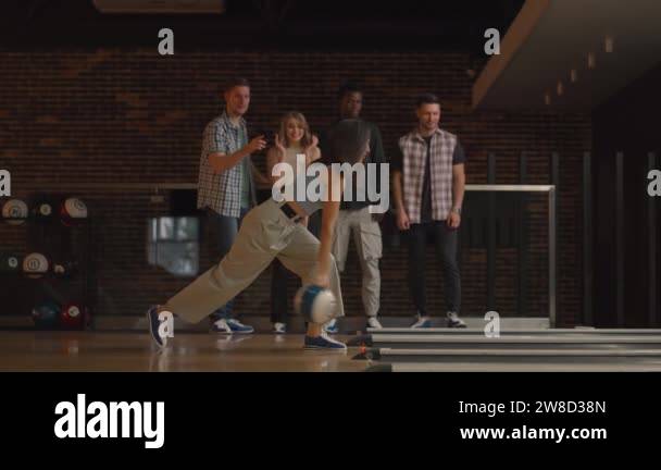 A young brunette woman makes the final throw with a bowling ball and ...