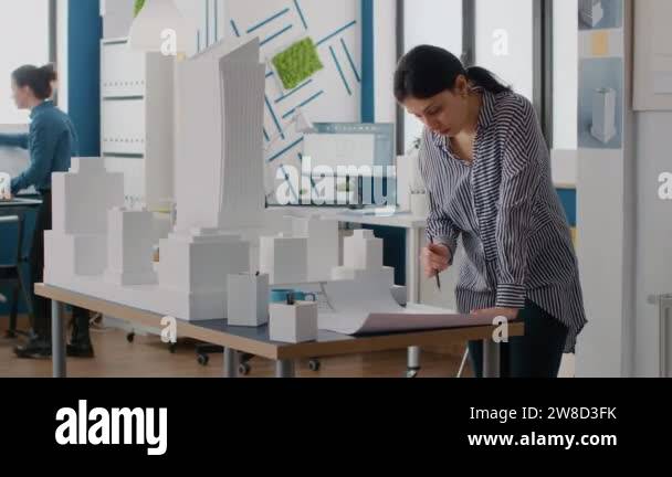 Woman Architect Analyzing Blueprints Plan On Table To Design Building Model And Maquette Stock