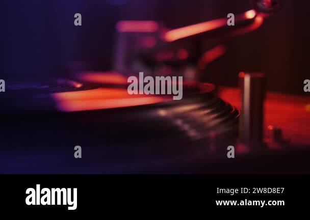A working record player. Man putting headshell on a vinyl record. Neon red illumination around ...